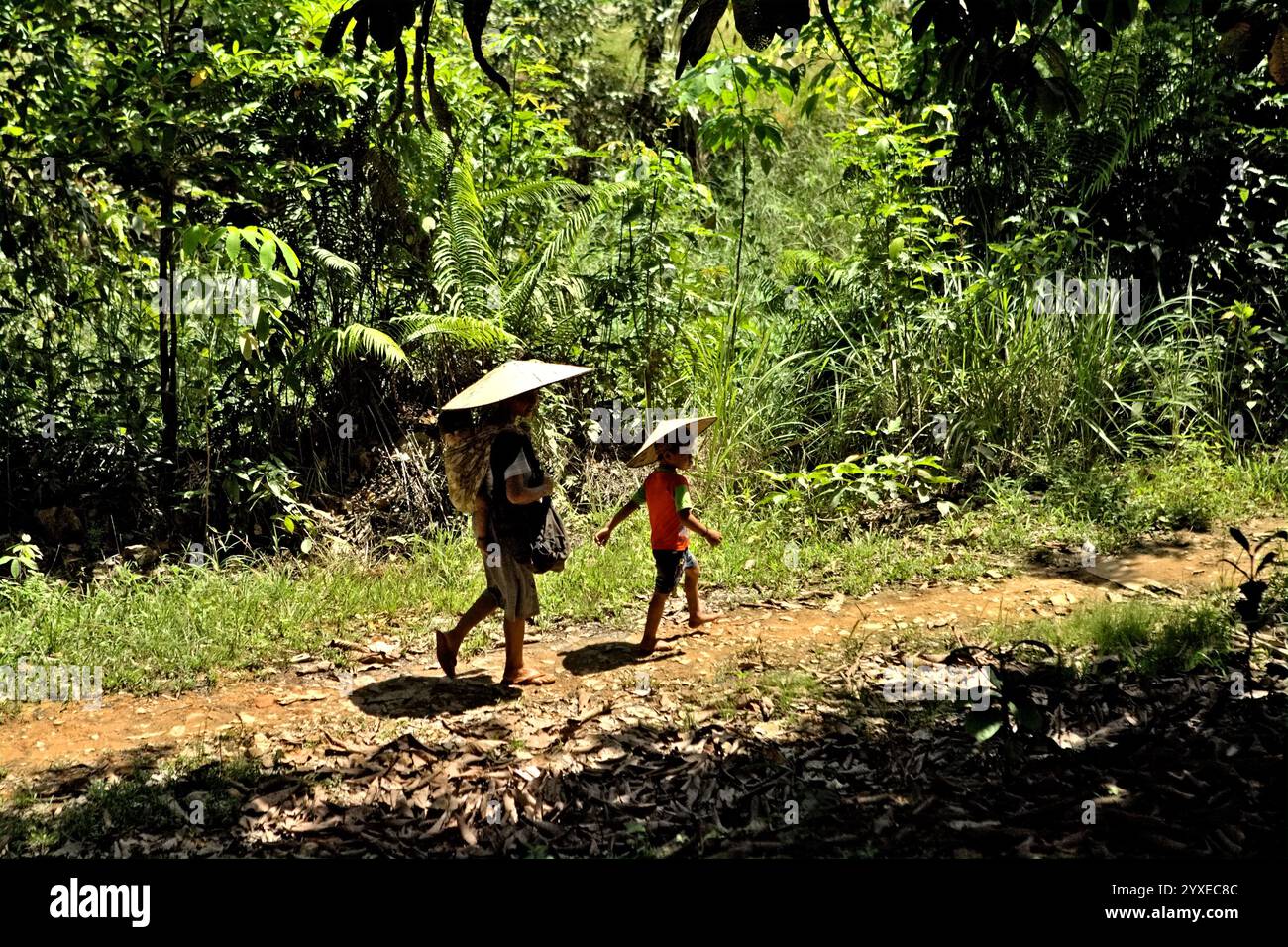 A woman and a child wearing conical hats as they are walking on rural ...