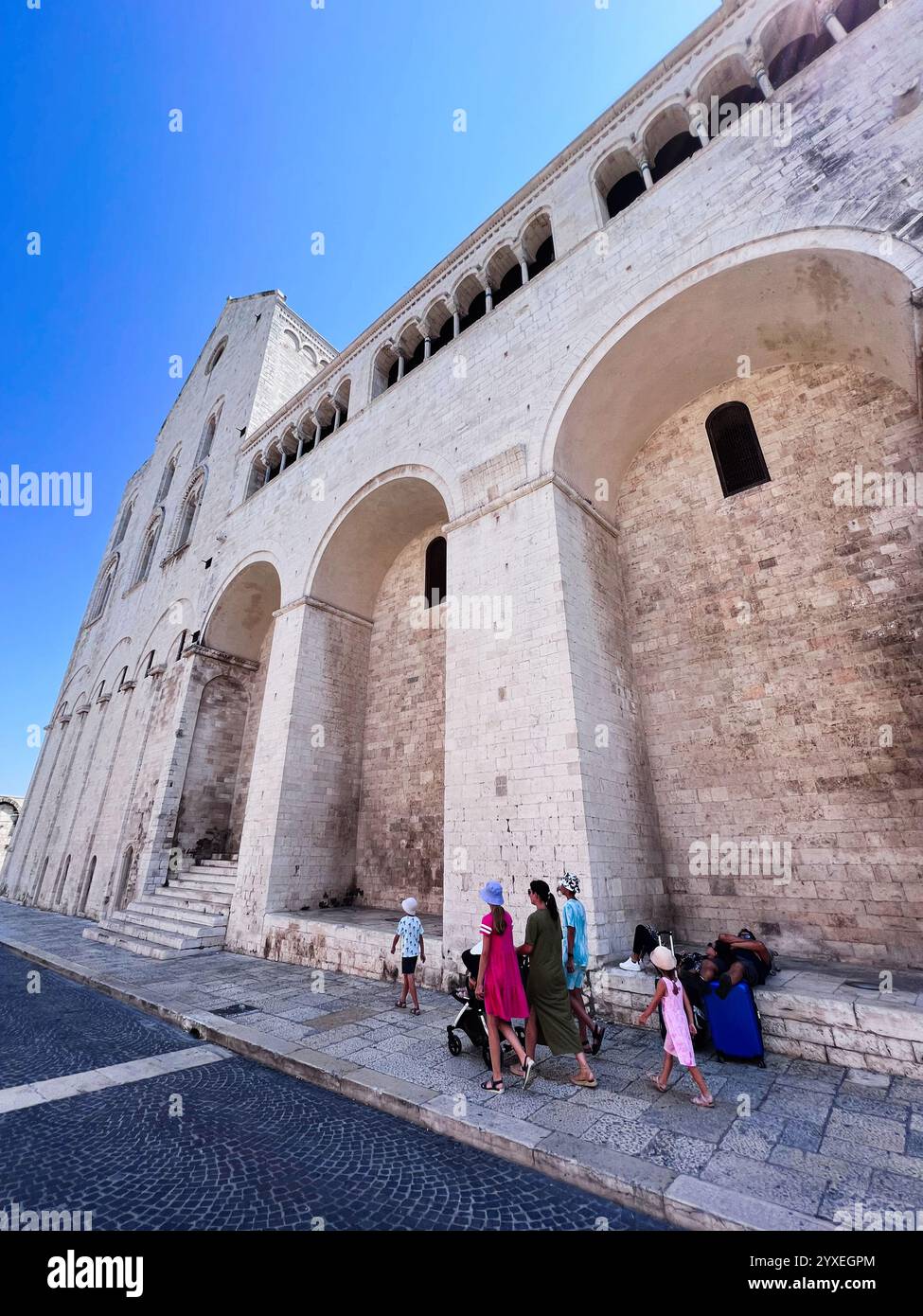 A family strolls beside an ancient, stone building under a clear sky ...