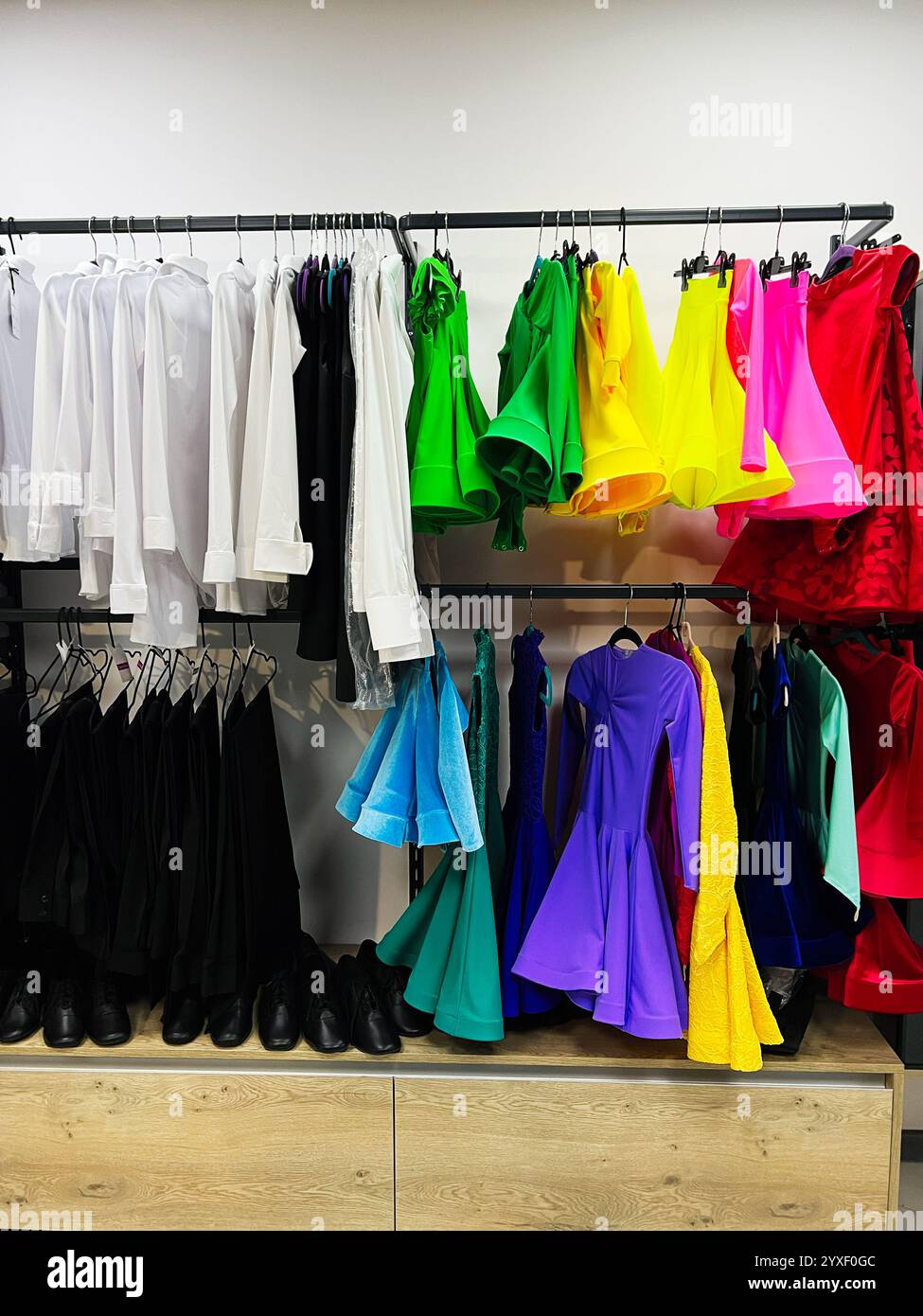 A selection of vibrant dance gowns and formal attire organized on racks ...