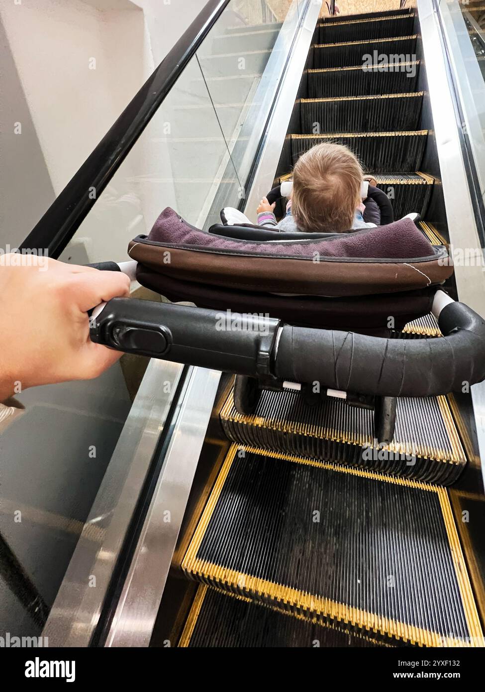 A rear view of a parent using an escalator while holding a baby ...