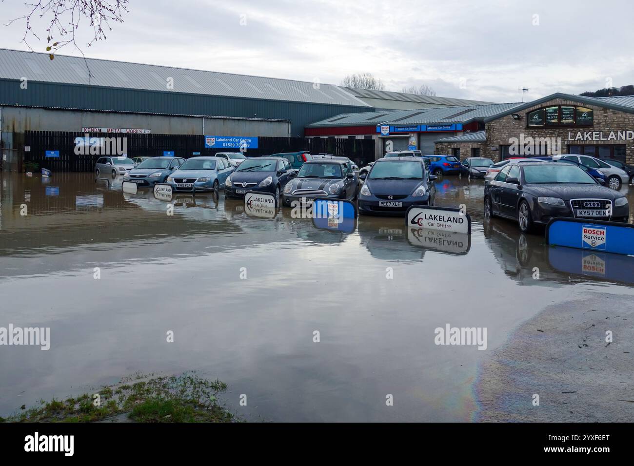 A flooded car sales forecourt and garage with cars partially submerged ...