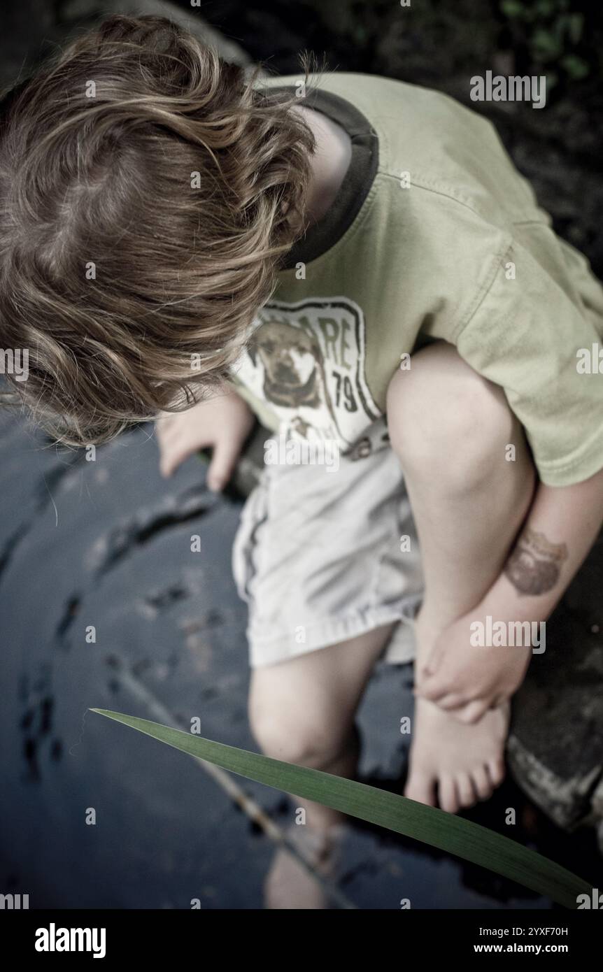 A young boy sitting by a pond Stock Photo - Alamy