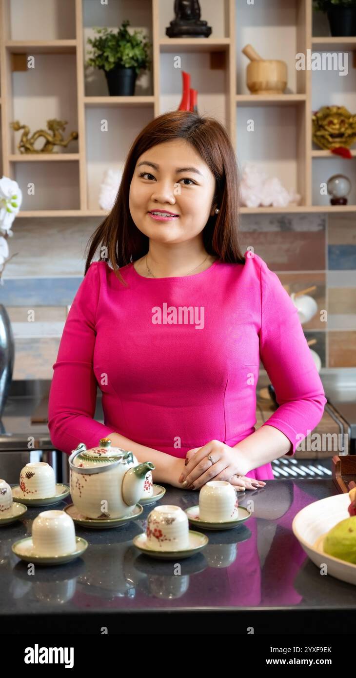 A nice Vietnamese young woman in a red dress smiles at the camera while standing behind the cafe ...