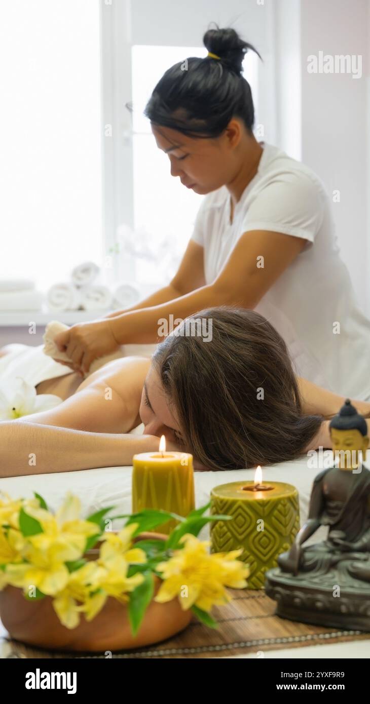 Female masseur using herbal compresses to massage the woman shoulder ...