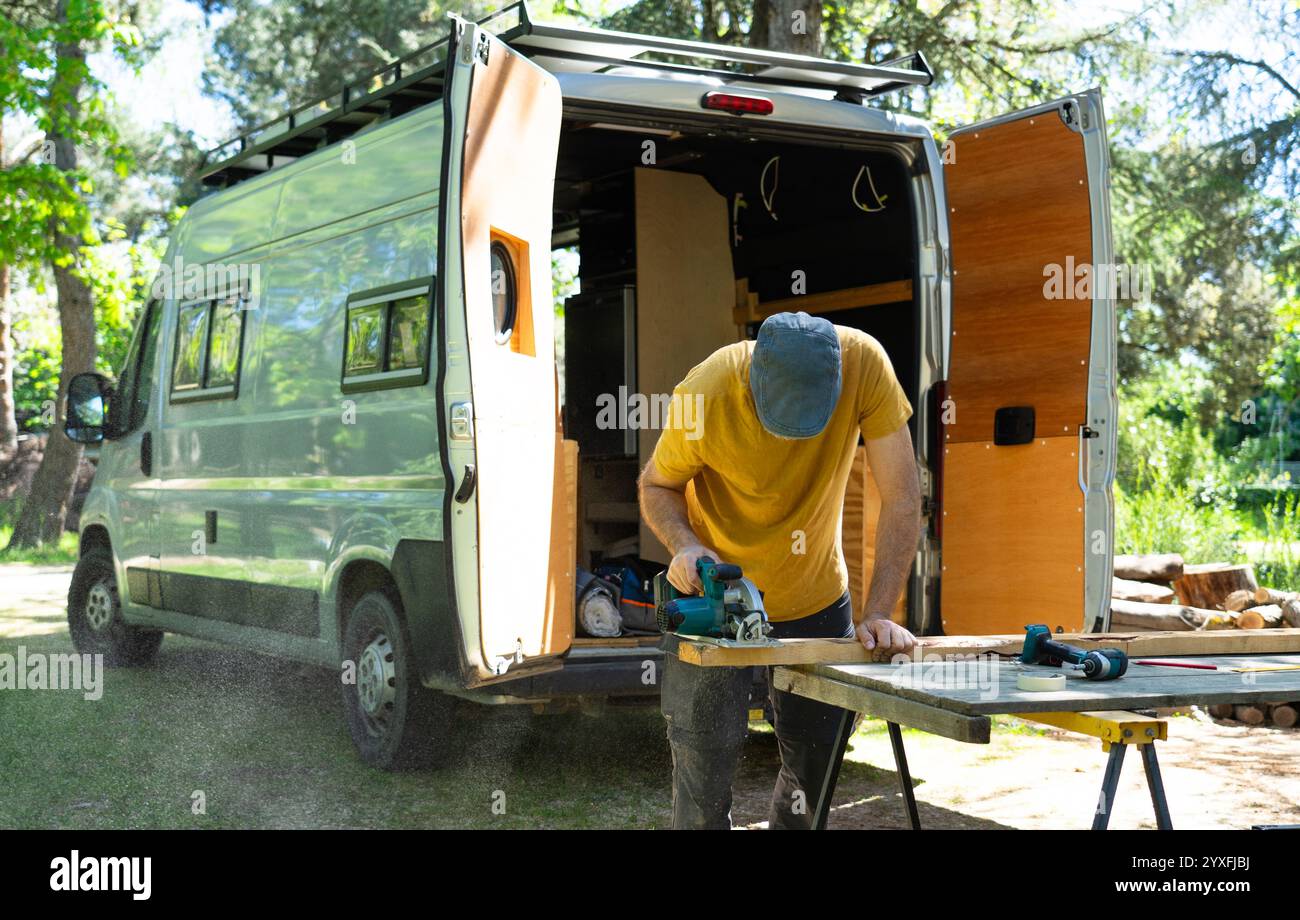 Carpenter using circular saw building furniture for his camper van conversion project, parked in ...