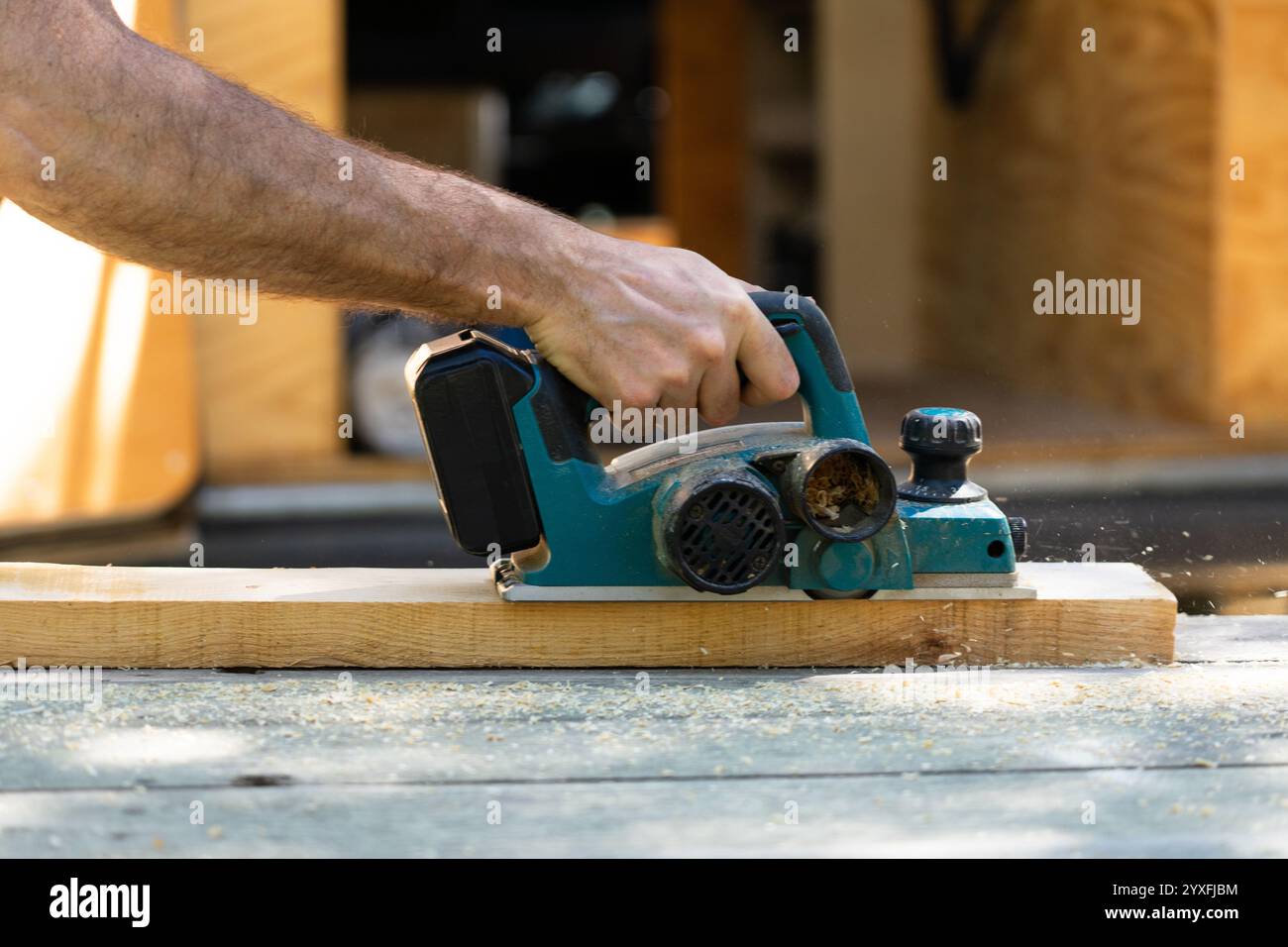 Carpenter using electric planer smoothing wooden plank in a workshop ...