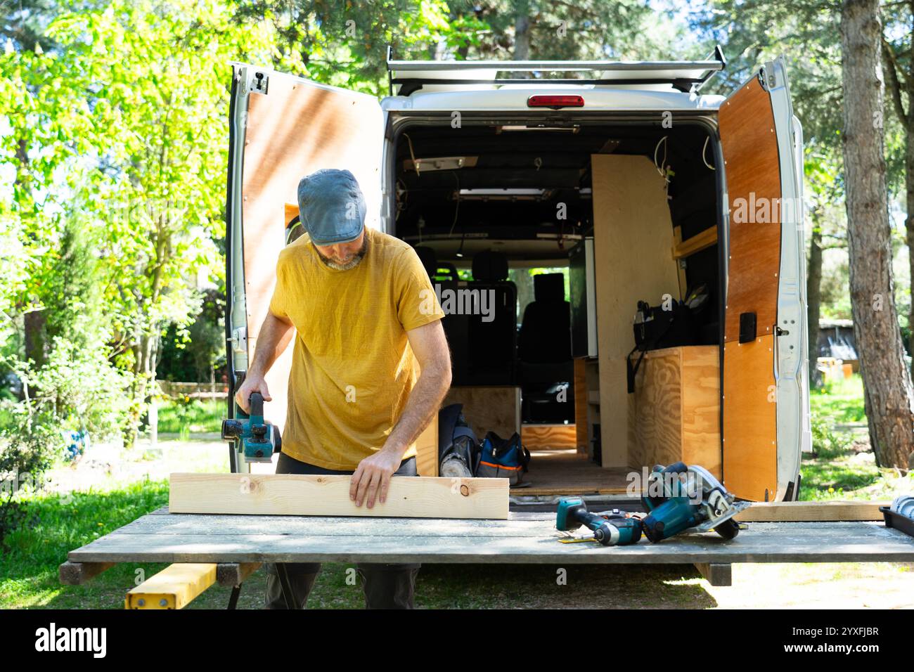 Carpenter using electric plane on wooden plank, constructing camper van ...