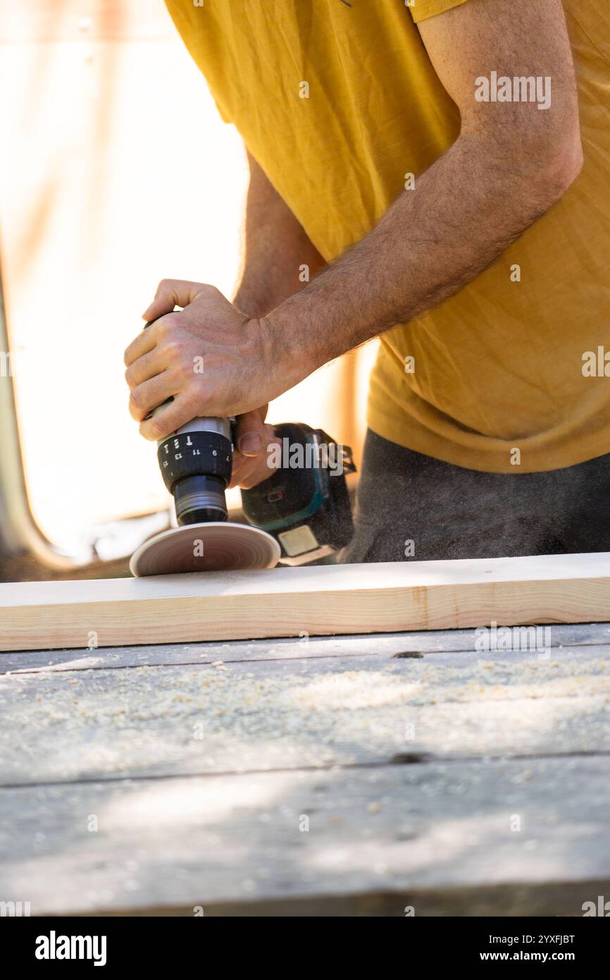 Carpenter sanding wooden plank outdoors using a cordless power tool ...