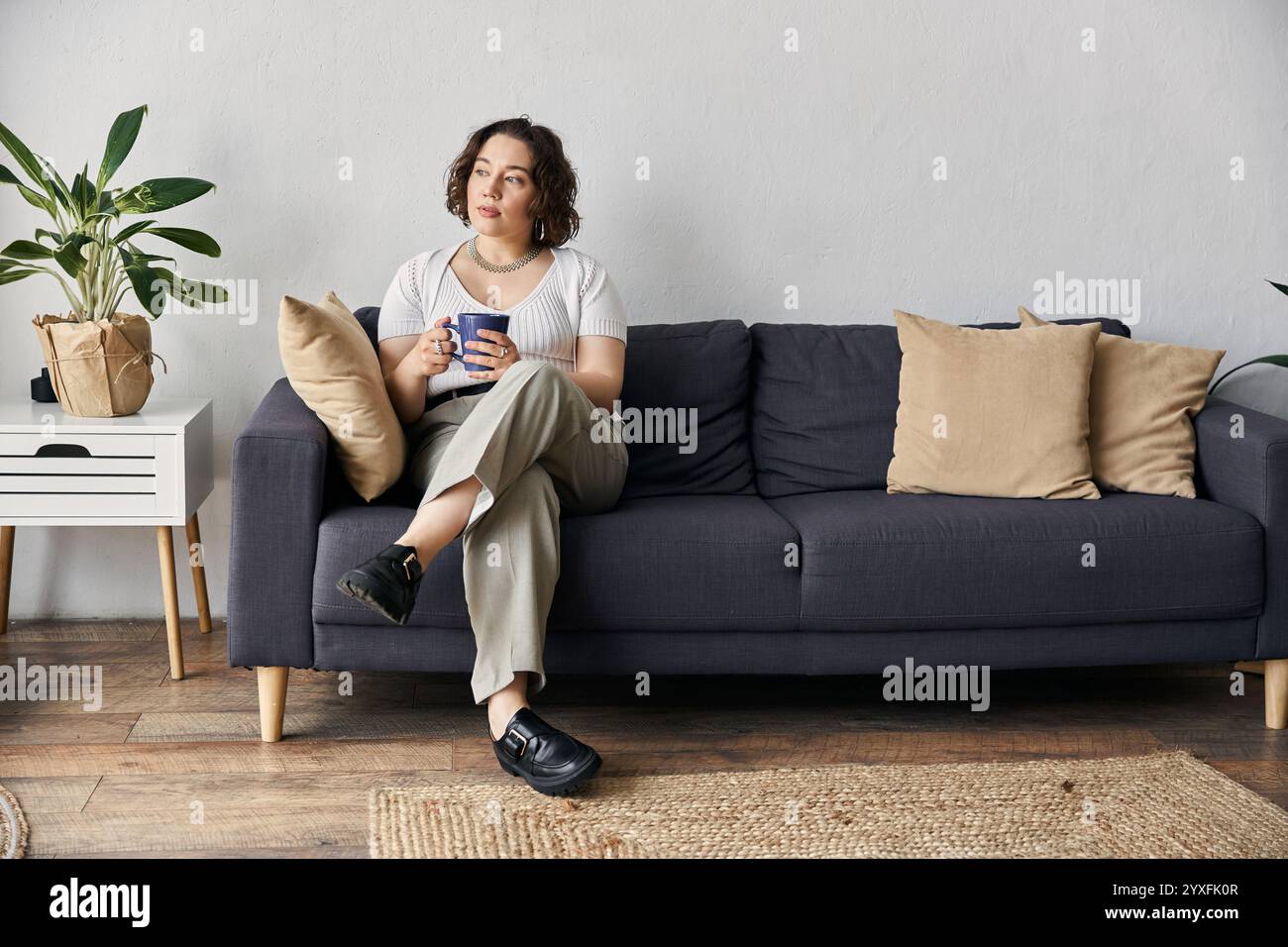 A beautiful young woman relaxes on a couch, sipping a warm drink in her ...
