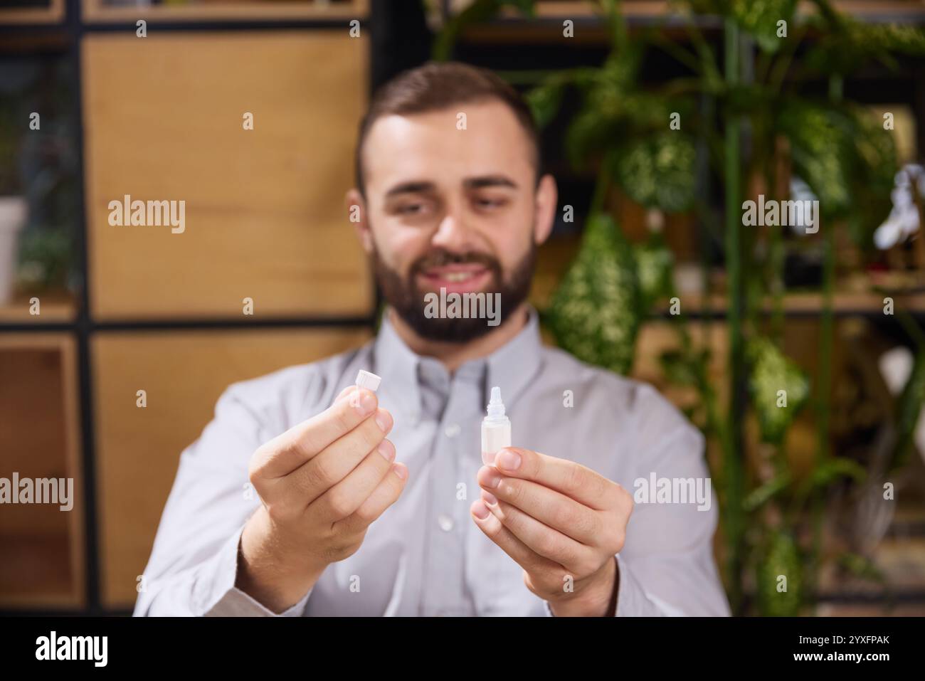 Young man opens bottle of eye drops and prepare to use them while ...
