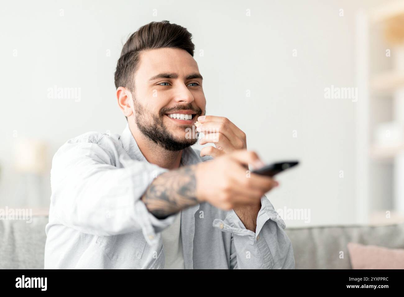 Happy relaxed guy watching Tv and eating popcorn, switching channels ...