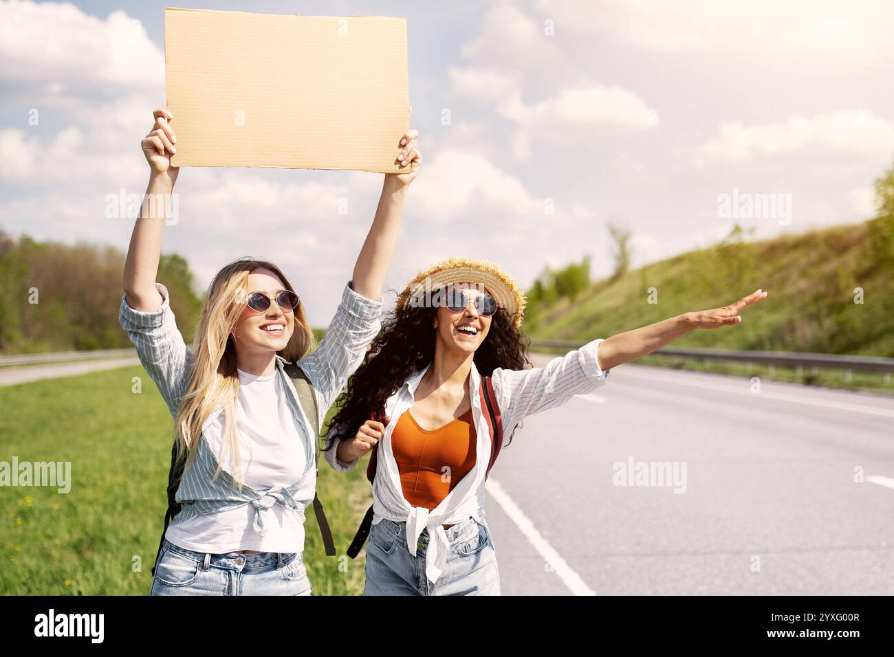 Two female friends hitching free ride, holding empty cardboard sign ...