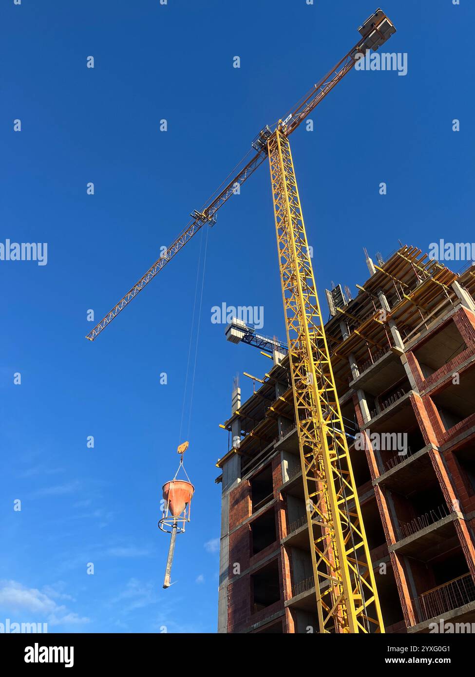 Tower crane lifting charging hopper at building construction site in ...