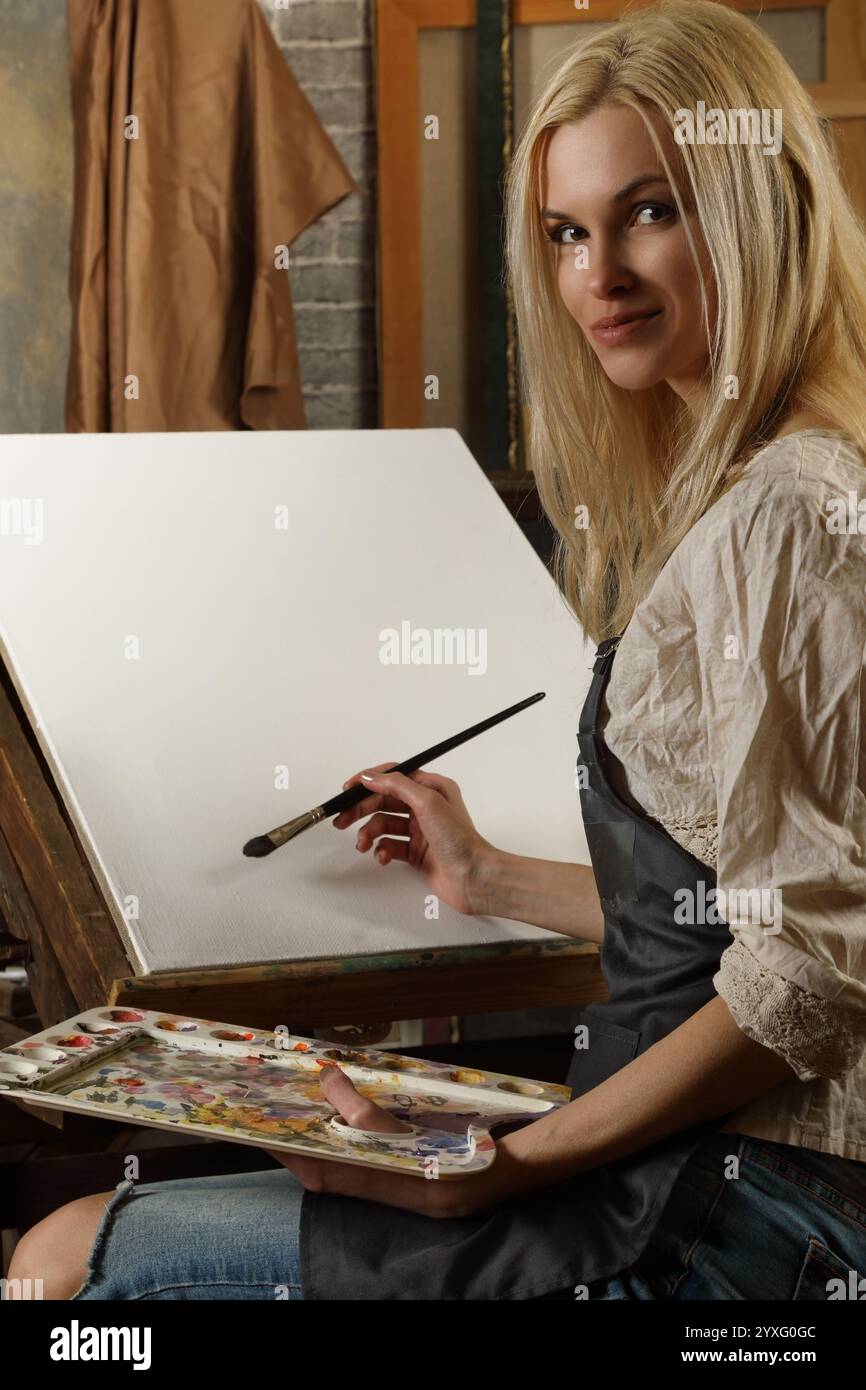 Young adult pretty female artist paints an oil painting in her artist's ...