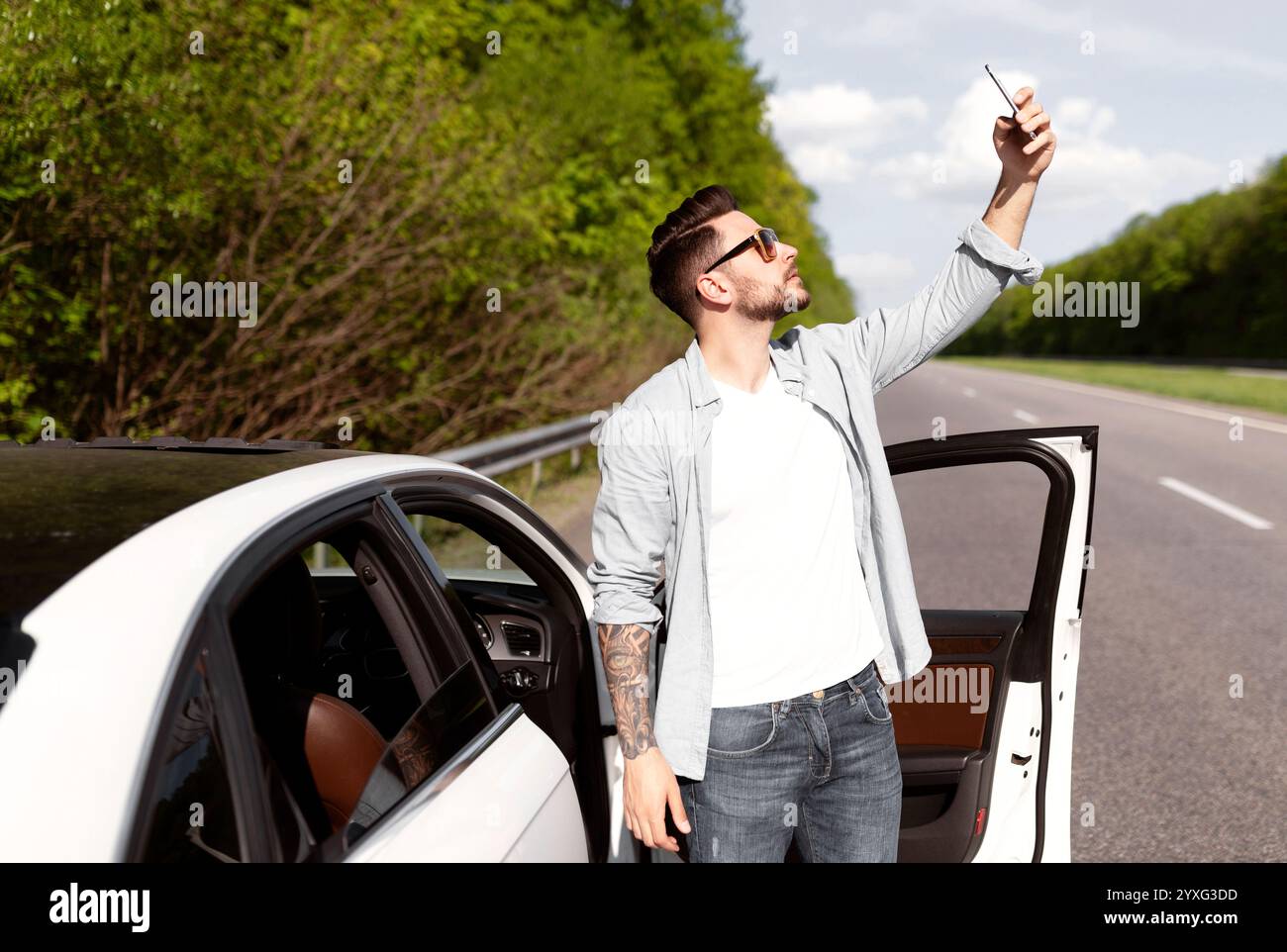 Stressed young guy standing near car with cellphone, having problem ...