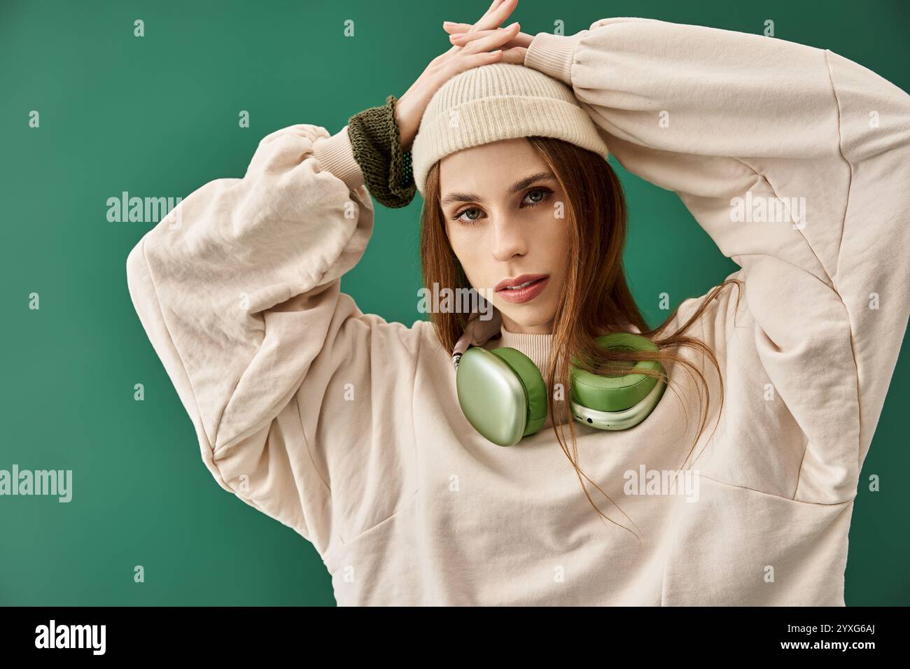 A young woman wearing a beanie and oversized sweater depicts her ...