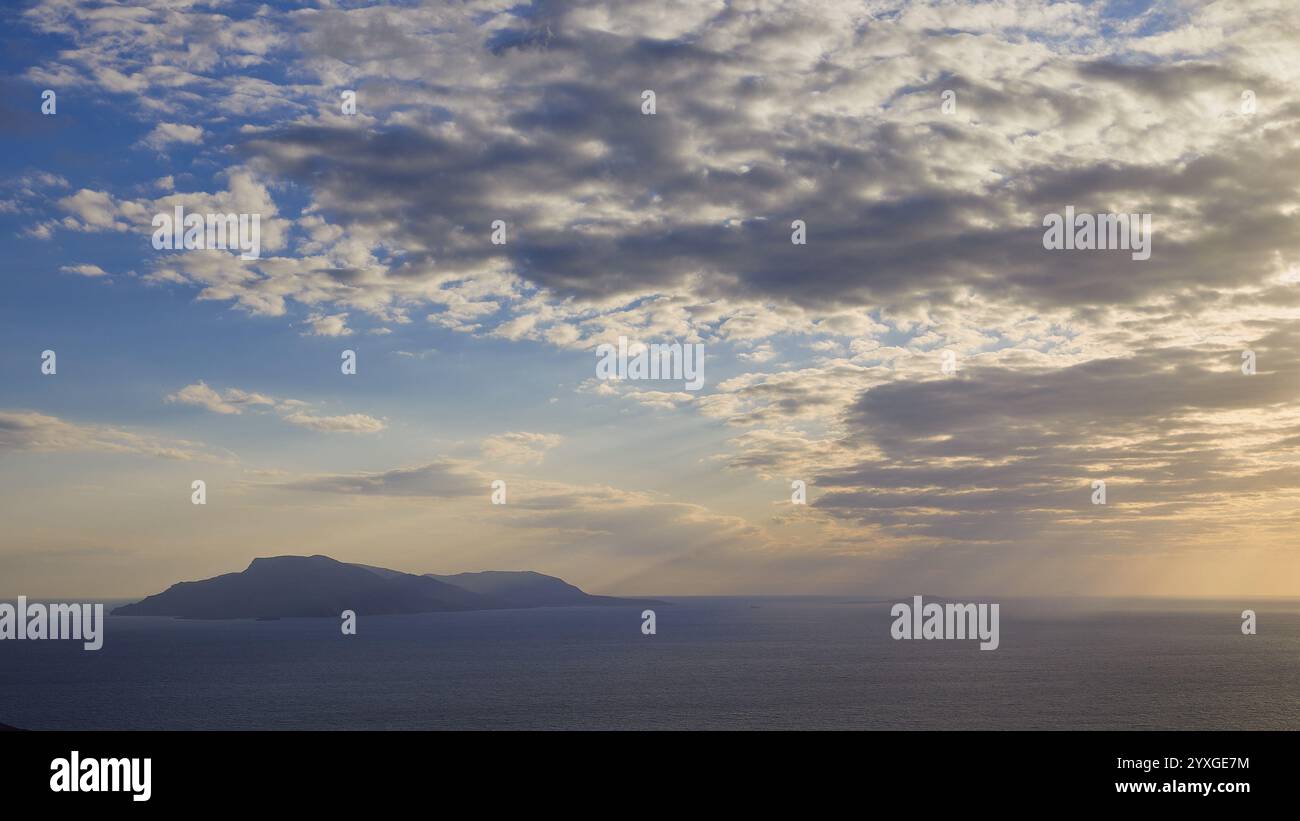 View of the sea and an island under a cloudy sky with rays of sunshine ...