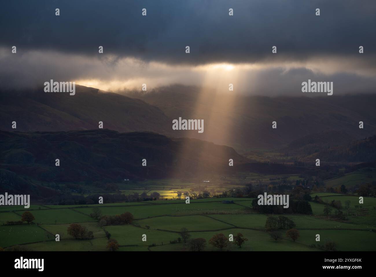 Beams of sunlight breaking through dramatic clouds over green fields in ...