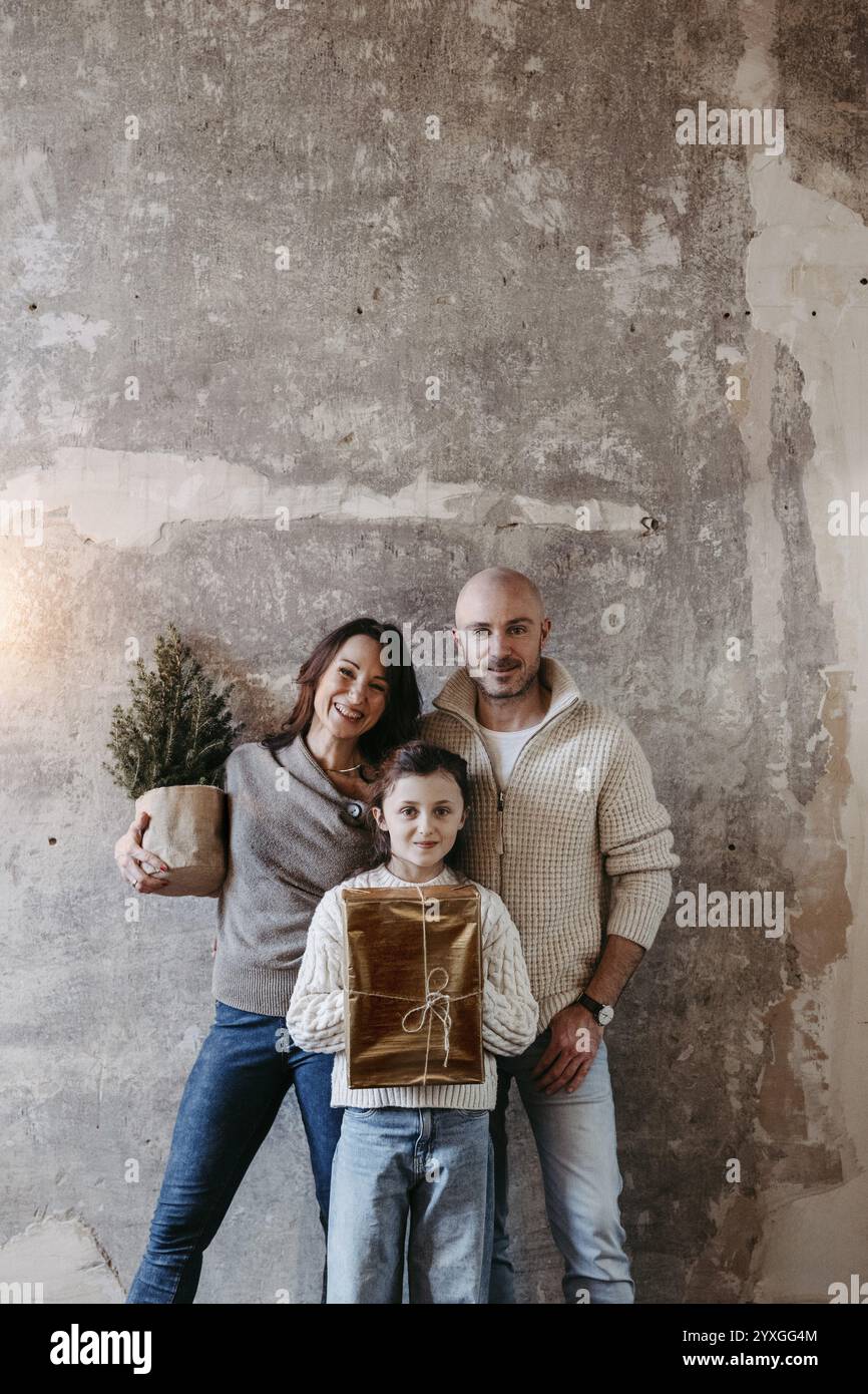 Family with a small Christmas tree and a present standing in front of a ...