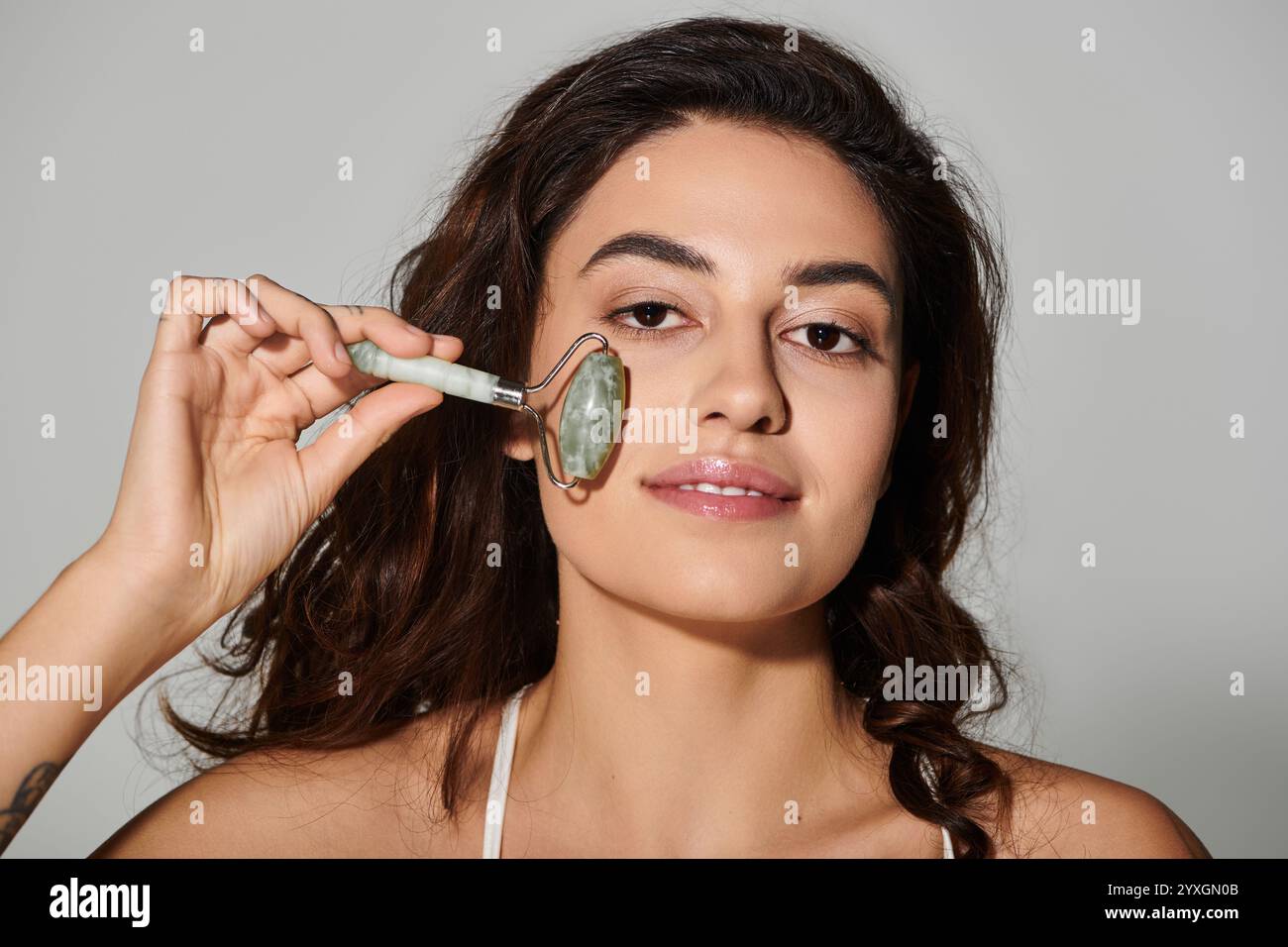 Woman enjoys skincare by using a jade roller on her face, enhancing her ...