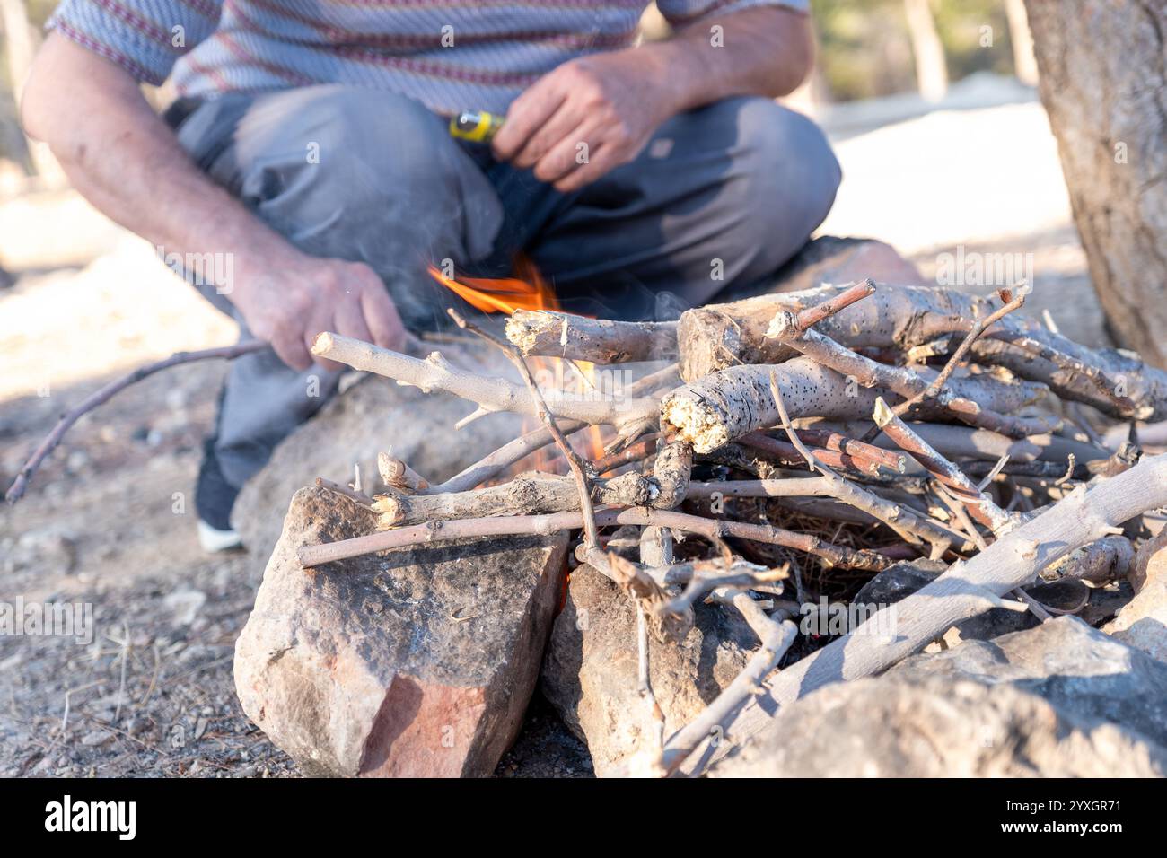 A close-up of a person igniting a campfire using twigs and sticks in an ...