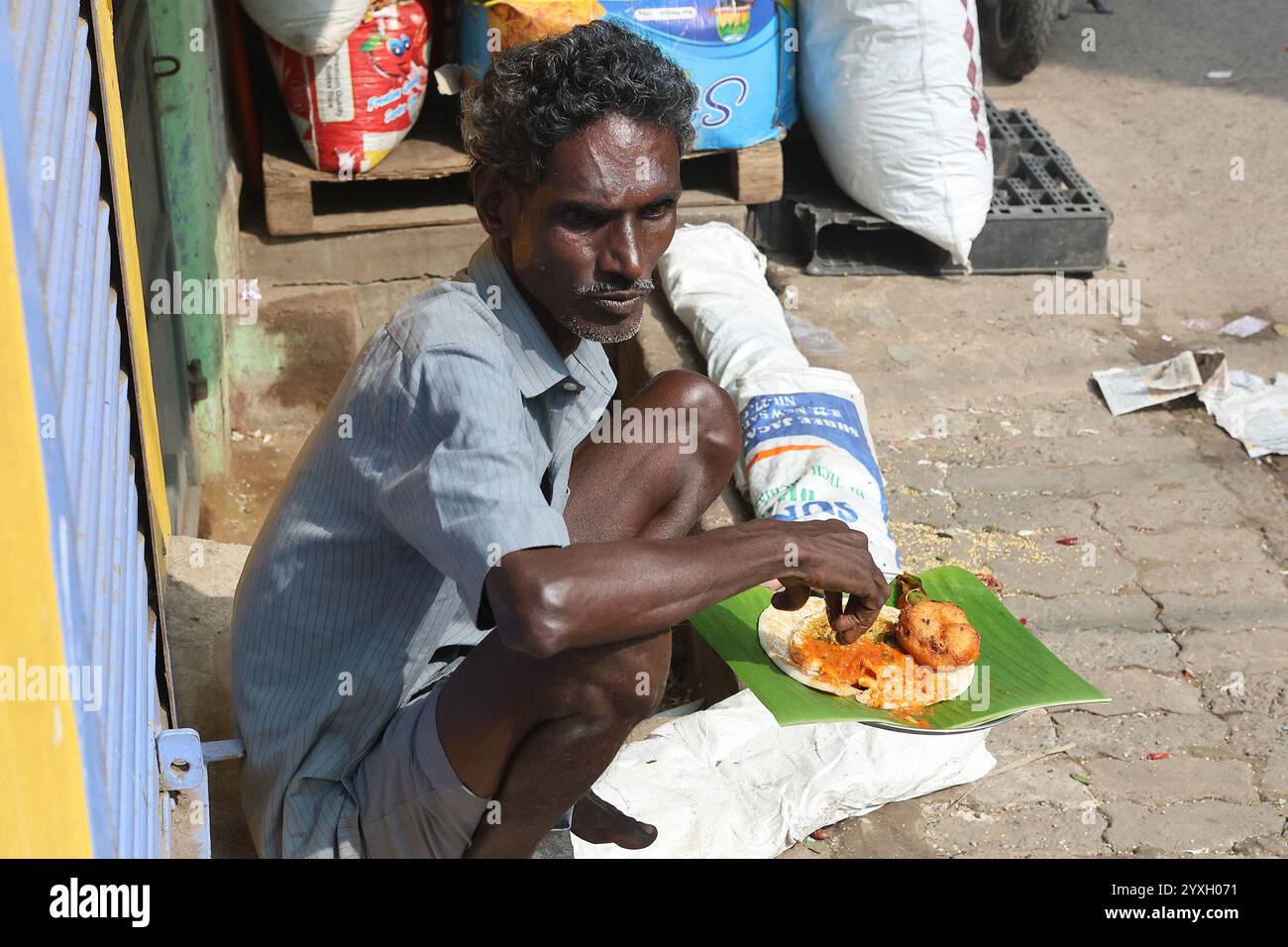 A man eating a snack of vada pav on the street in Chennai, Tamil Nadu ...