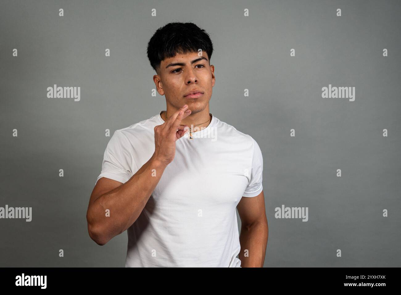 Young latino man making a hand gesture, possibly a money sign, while ...