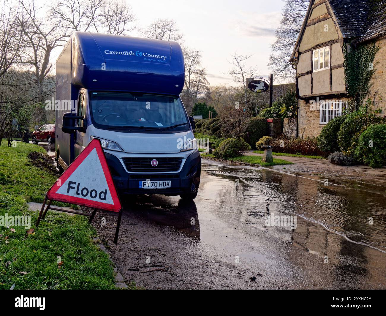 Flood warning sign on side of the road in front of removal van with ...