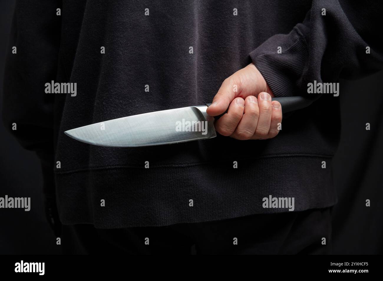 Criminal hiding a knife behind his back, man holding a weapon closeup ...