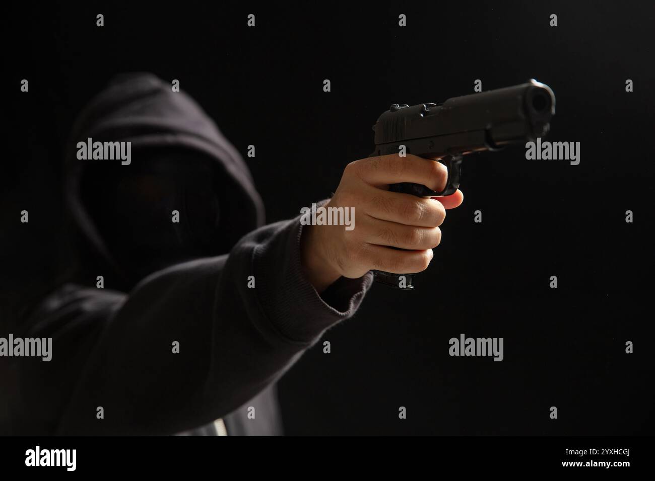 Robber wearing black hood holding gun, ready to shoot. Armed gangster ...