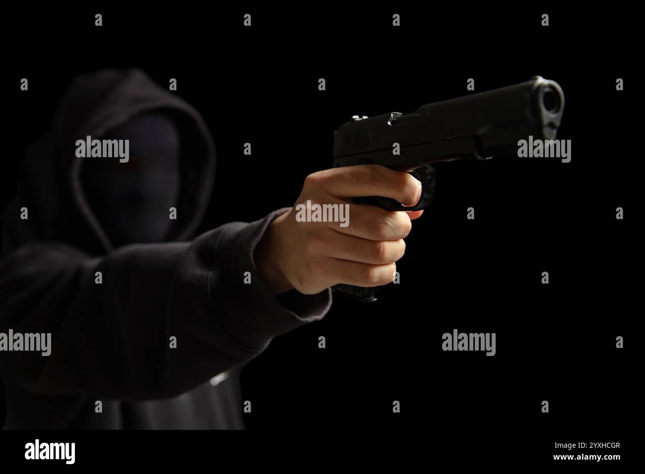 Robber wearing black hood holding gun, ready to shoot. Armed gangster ...