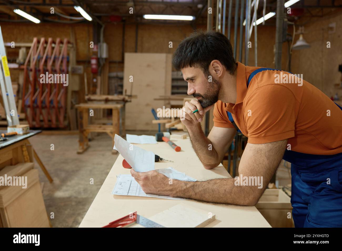 Pensive man carpenter reading blueprints and thinking during ...