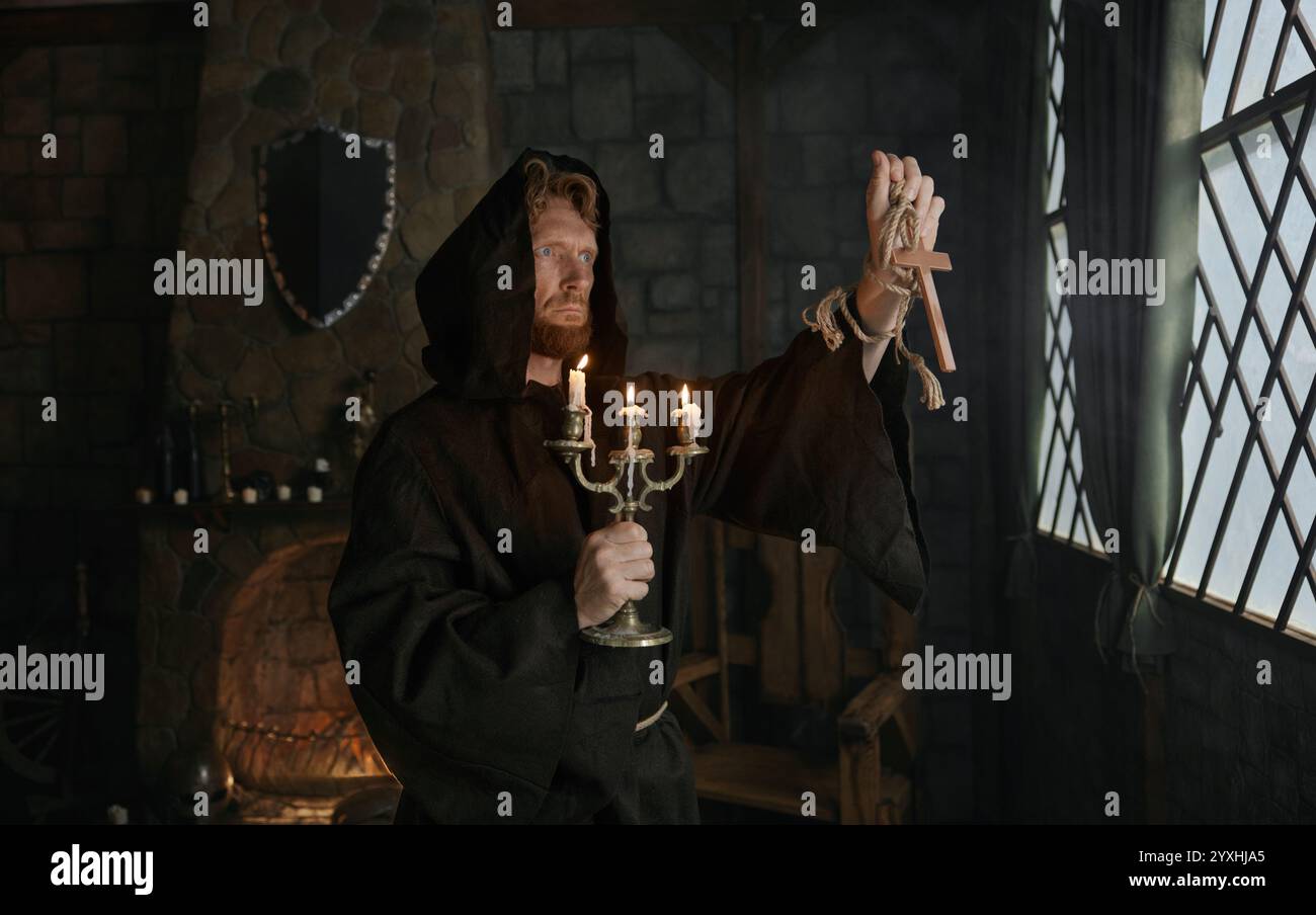 Portrait of hooded monk in medieval costume holding wooden cross and ...
