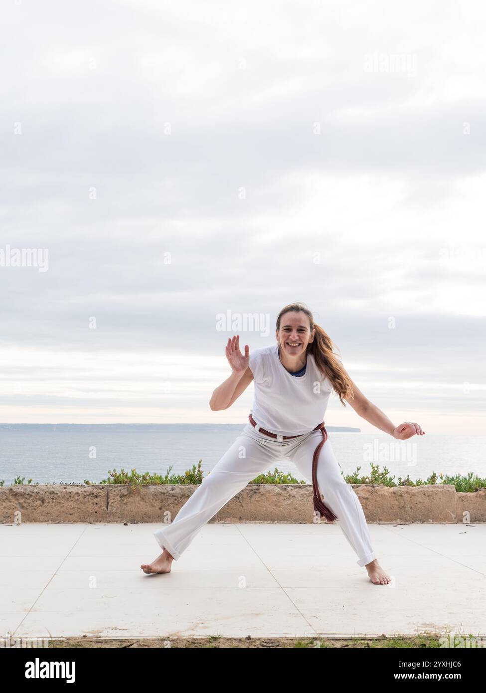 Woman practicing capoeira martial arts outdoors with a serene ocean ...