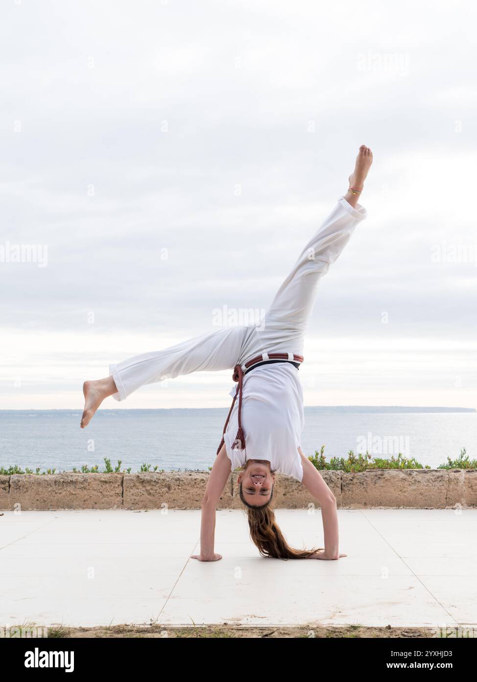 A woman practicing capoeira handstand outside by the sea, showcasing ...