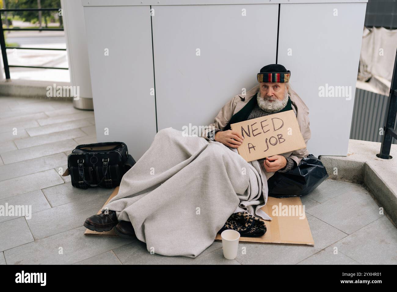 Wide shot of tired elderly homeless man holding NEED JOB sign in city ...
