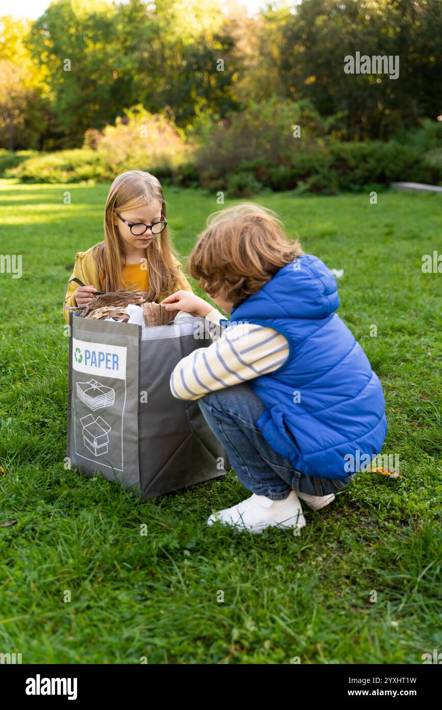 Little children picking up paper trash in a park participating in a ...