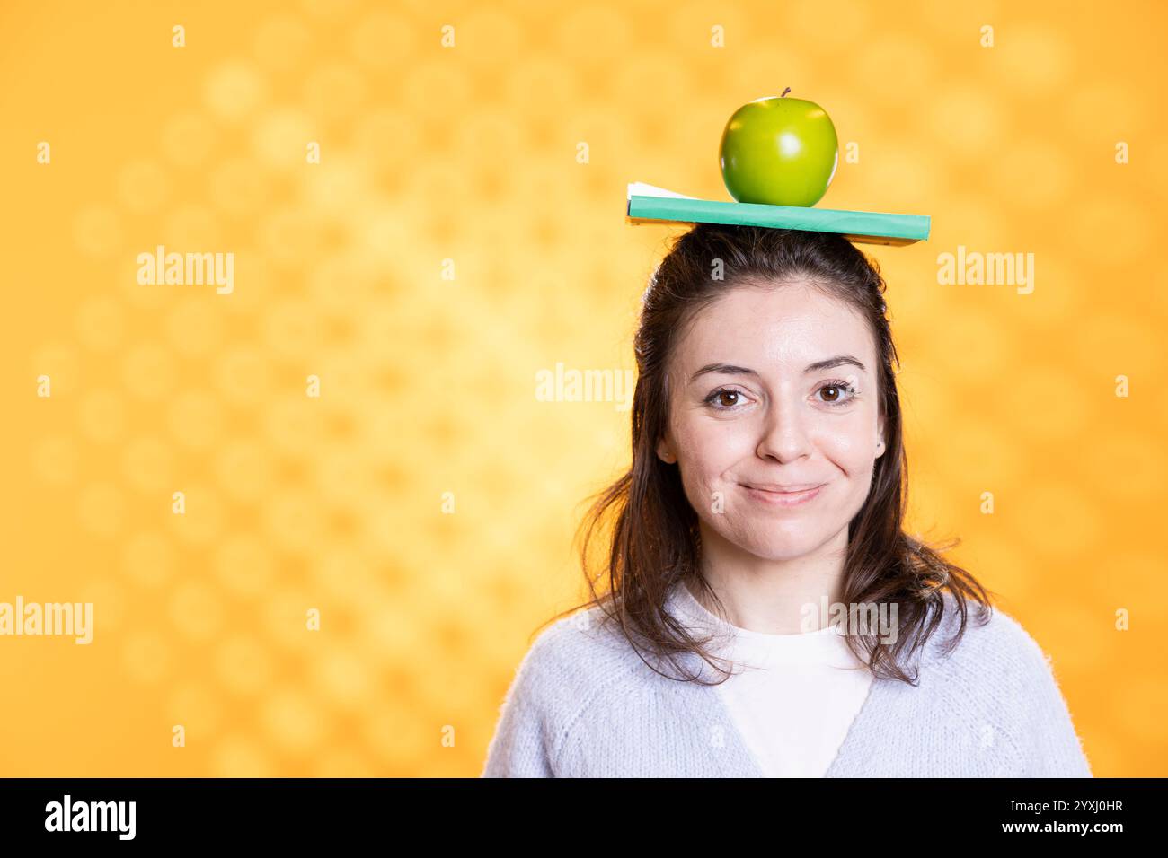 Portrait of jolly woman placing book on head and apple, acting quirky ...