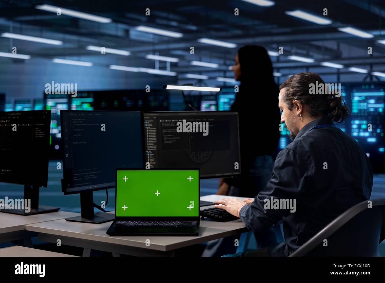Admin in data center uses green screen laptop to update systems, protecting servers from ...