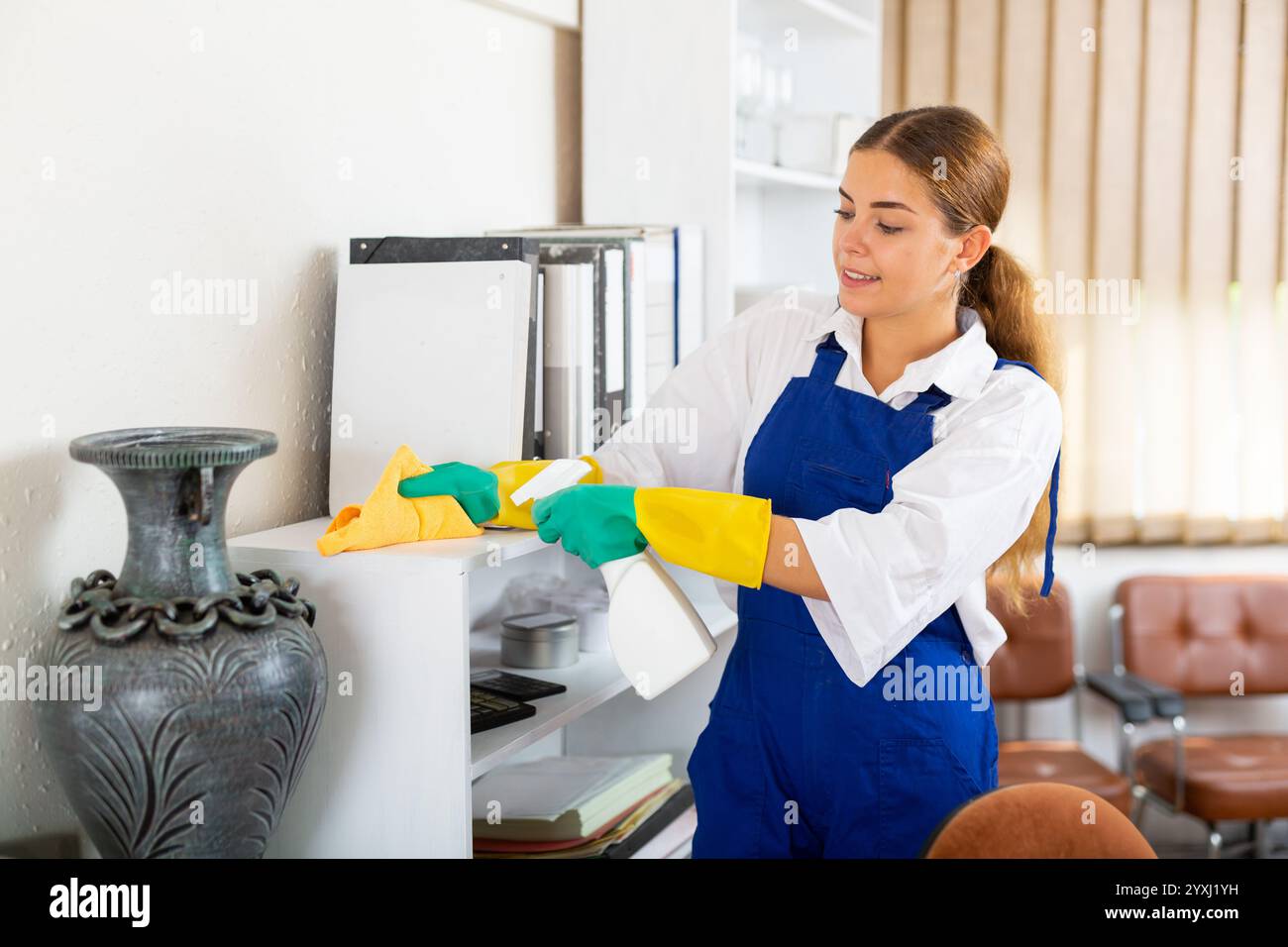 Professional female worker of office cleaning service wiping furniture ...