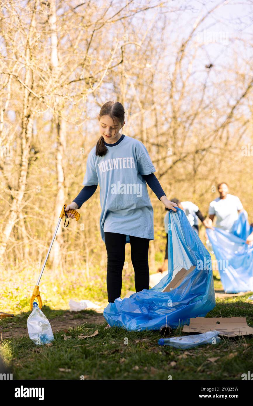 Young kid volunteer collecting garbage in blue disposal bags, clearing ...