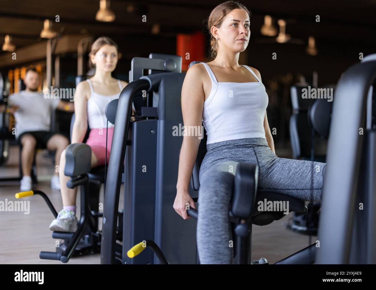 Slender athletic girl work out muscles of legs and thighs on simulator ...