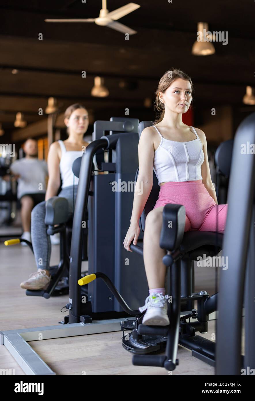 Slender athletic girl work out muscles of legs and thighs on simulator ...