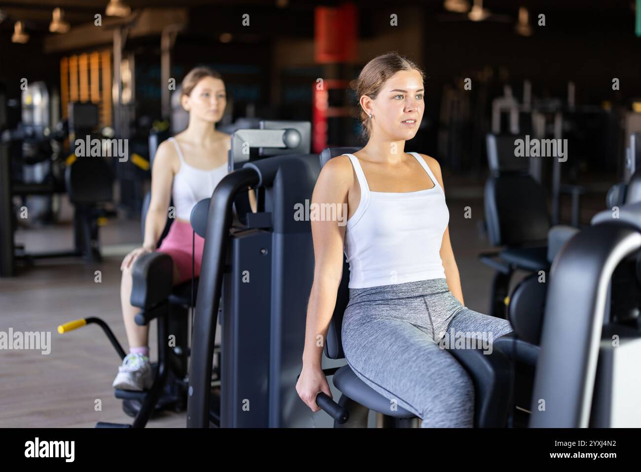 Slender athletic girl work out muscles of legs and thighs on simulator ...