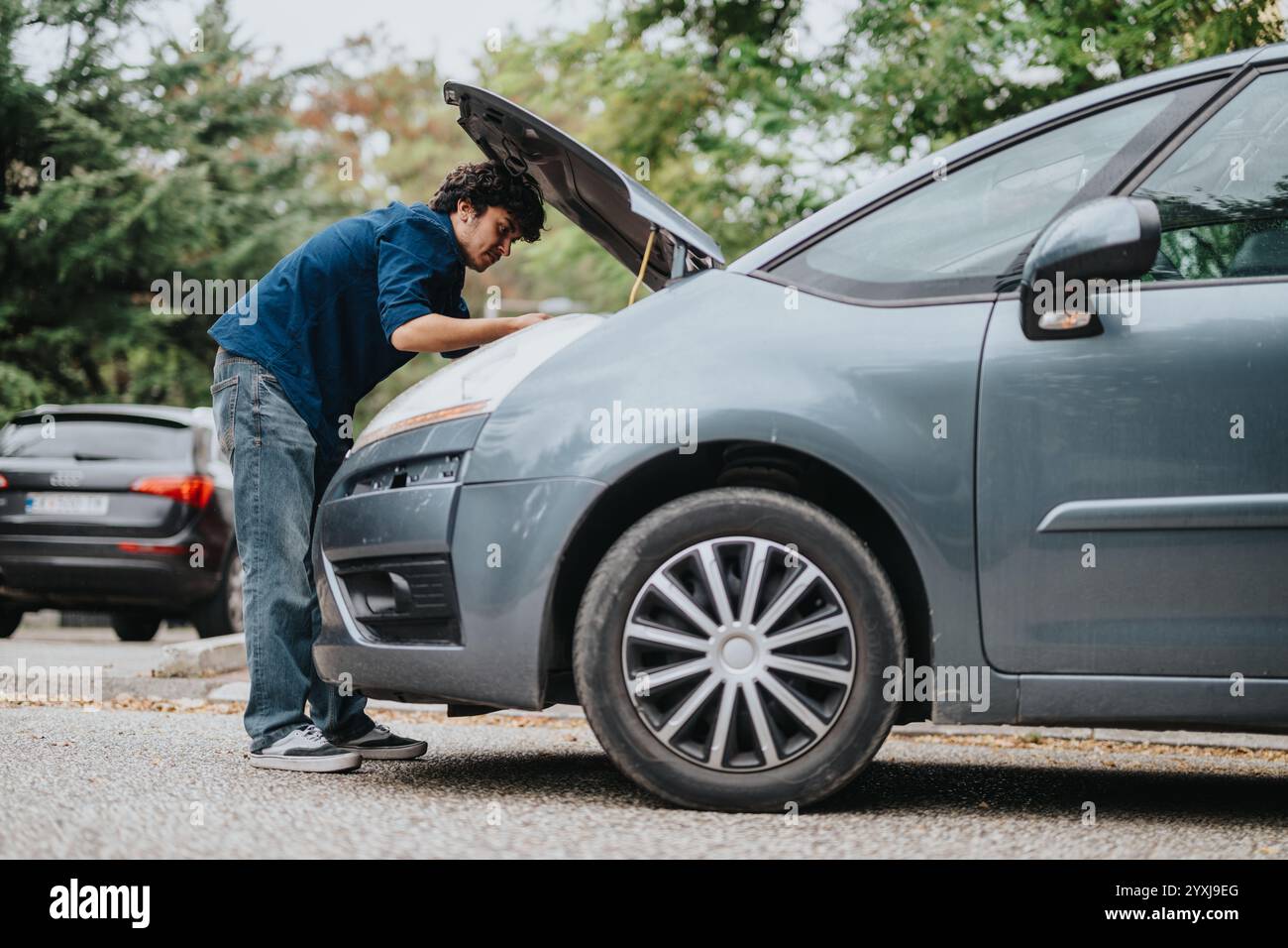 Man inspecting car engine with open hood in a park setting Stock Photo ...