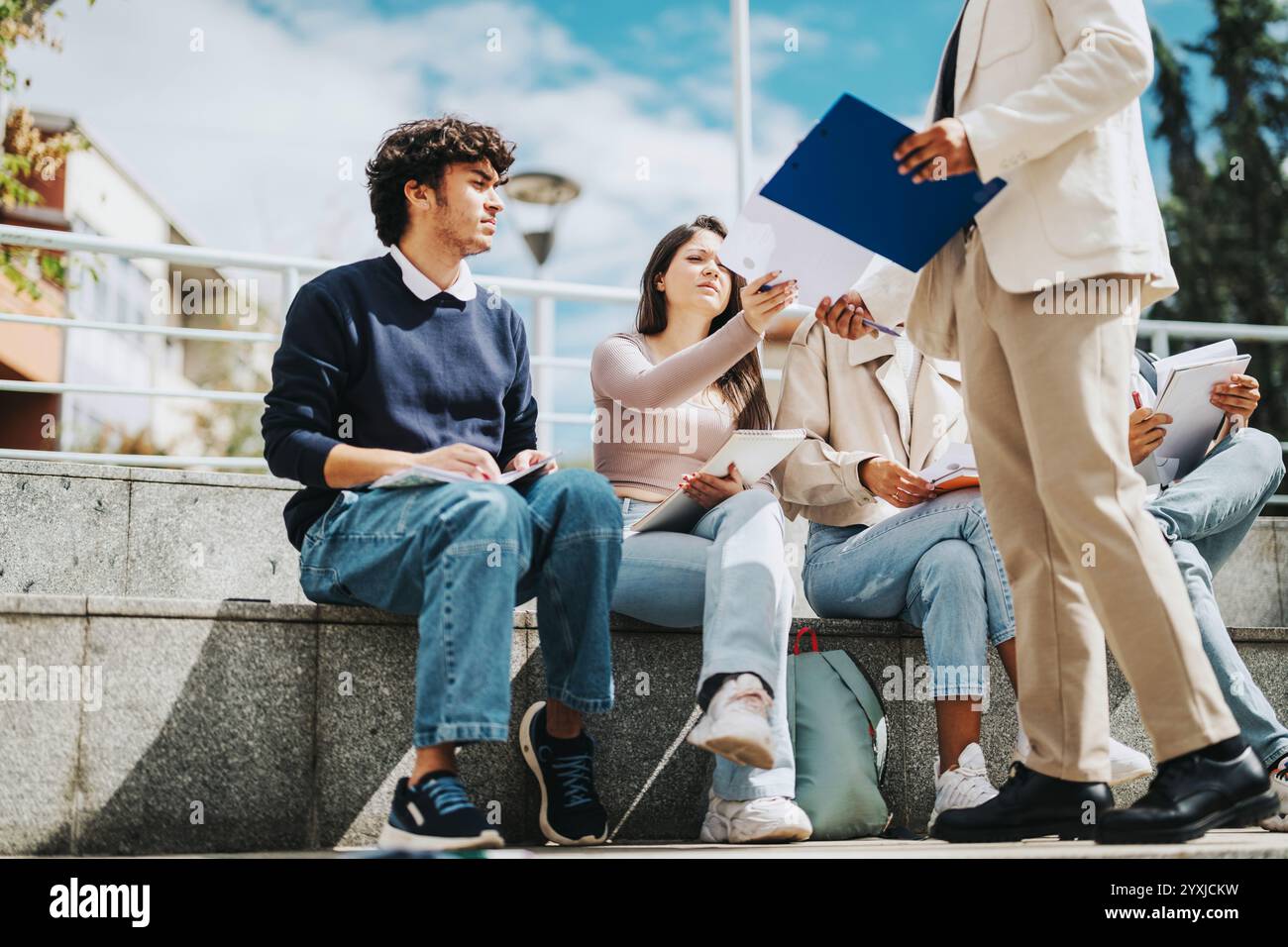 High school students studying outdoors with a teacher's assistance ...