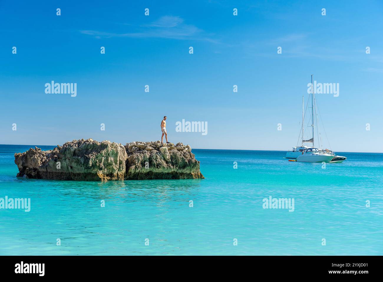 Idyllic scenery of clear blue sea with rock on the left and catamaran ...