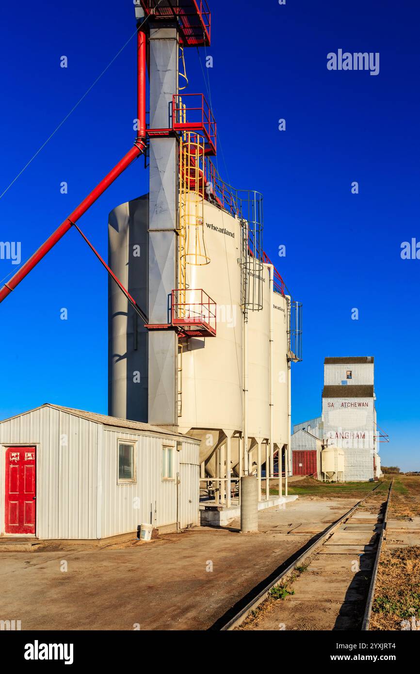 A grain silo is next to a small building. The silo is tall and white ...