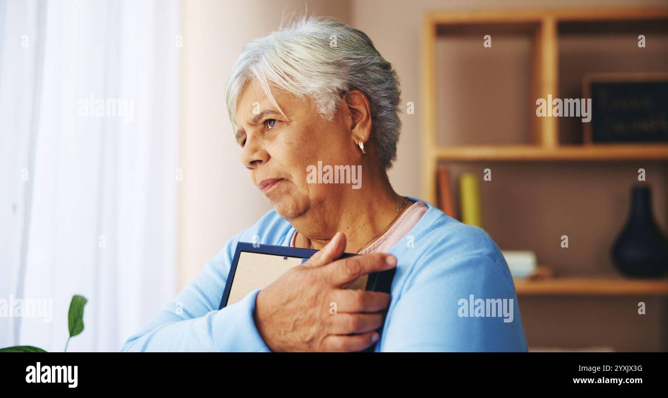 Senior woman, photo frame and memory in home with grief, thinking and remember loss in living ...