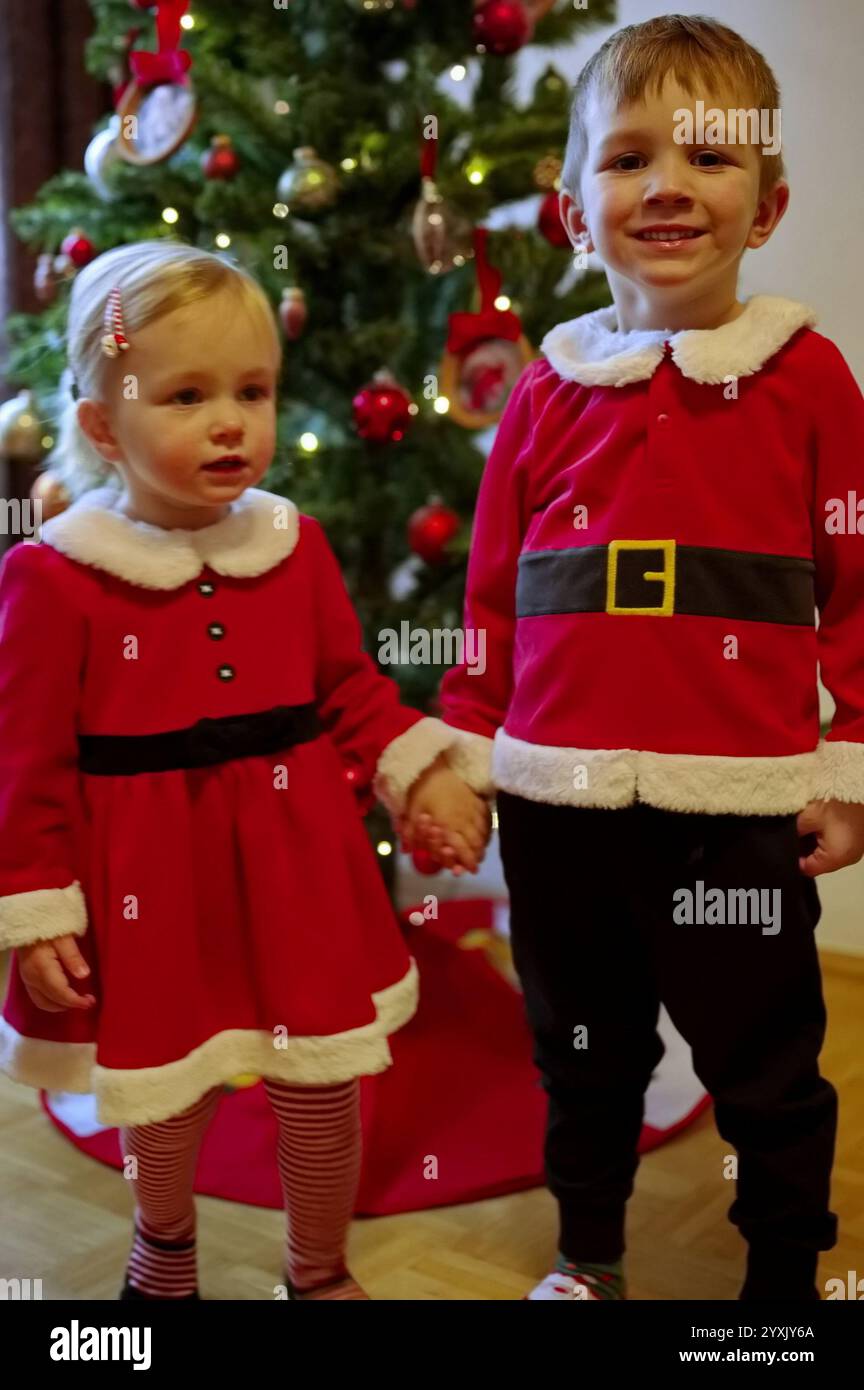 Cute little children standing in front of Christmas tree Stock Photo ...